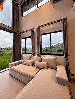 Uma sala de estar moderna com um sofá modular, janelas amplas e vista para uma paisagem verde.