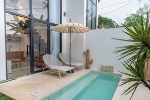 Uma área de piscina moderna ao ar livre, com estrutura de vidro, um guarda-sol branco e uma planta cacto.