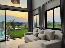 Uma sala de estar moderna com uma janela grande, um sofá e vista para uma piscina e vegetação.