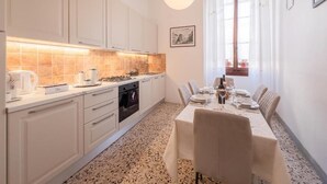 Uma cozinha moderna com armários brancos, uma mesa de jantar posta para seis pessoas e uma janela grande com cortinas.