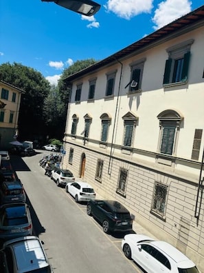 Vista da rua com carros estacionados e um edifício com várias janelas e persianas.