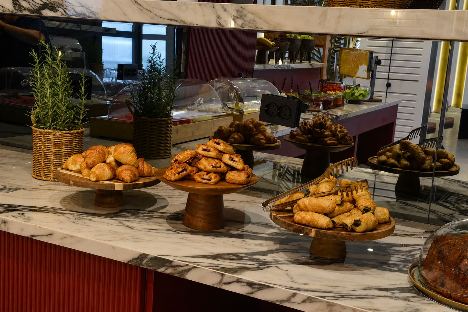 Balcão de buffet com diversos produtos de panificação e uma planta decorativa.
