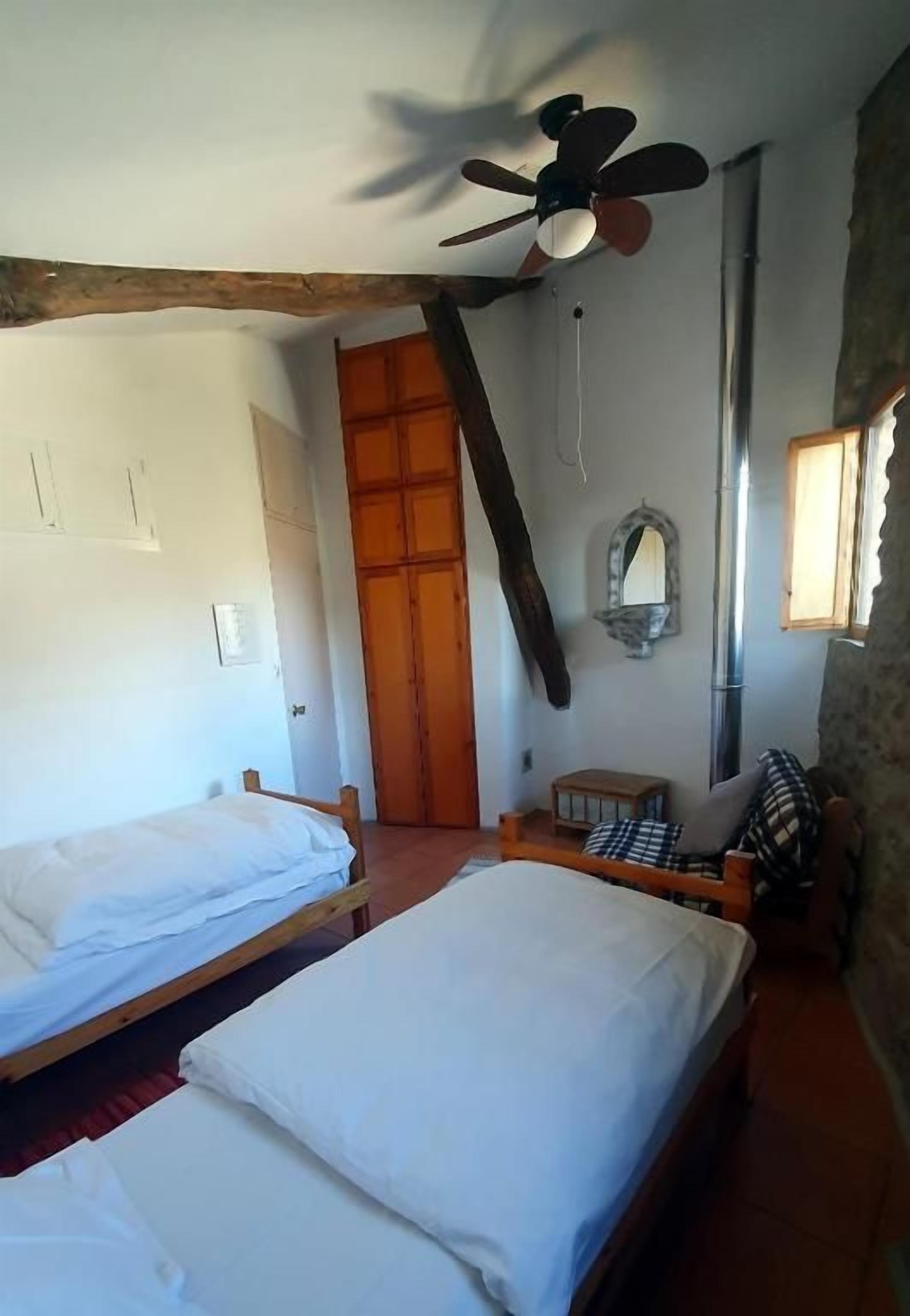 Quarto com duas camas de solteiro, um ventilador de teto, uma porta de madeira e uma janela.