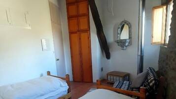 Quarto com duas camas de solteiro, um ventilador de teto, uma porta de madeira e uma janela.