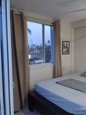 Quarto com cama, janela com cortinas, um quadro na parede e uma porta.
