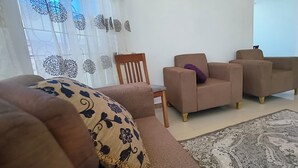 Uma sala de estar com sofá, duas poltronas, uma cadeira de madeira e um tapete estampado.
