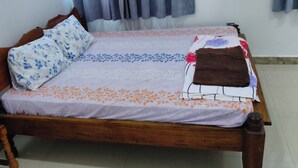 Uma cama de madeira com colcha florida, um travesseiro e um cobertor dobrado.