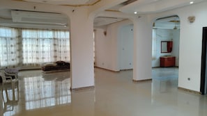 Um quarto espaçoso com teto alto, sofá, uma cadeira e toucador com espelho.