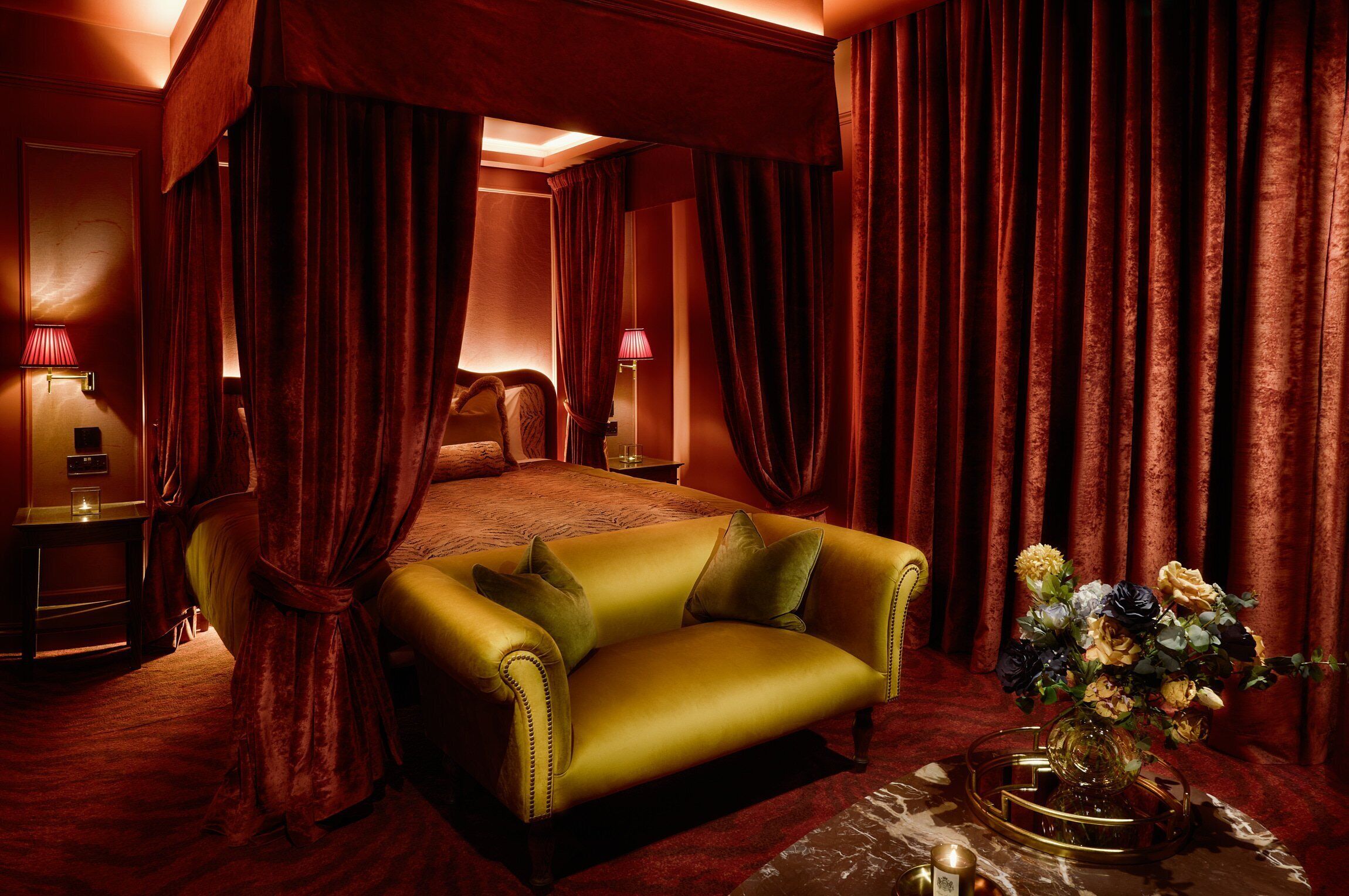 Um quarto luxuoso com uma cama de dossel, um sofá verde e um vaso de flores.
