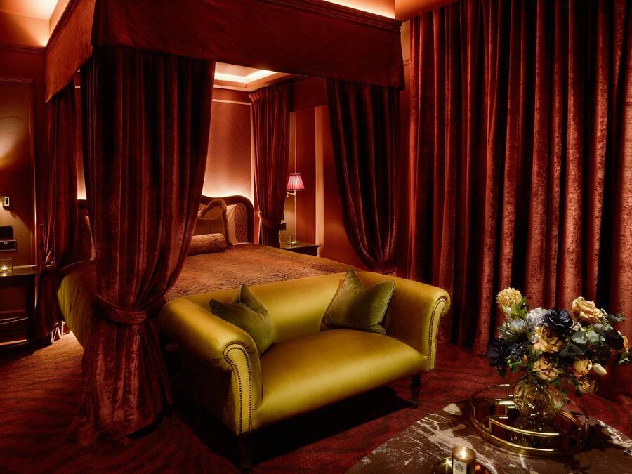Um quarto luxuoso com uma cama de dossel, um sofá verde e um vaso de flores.