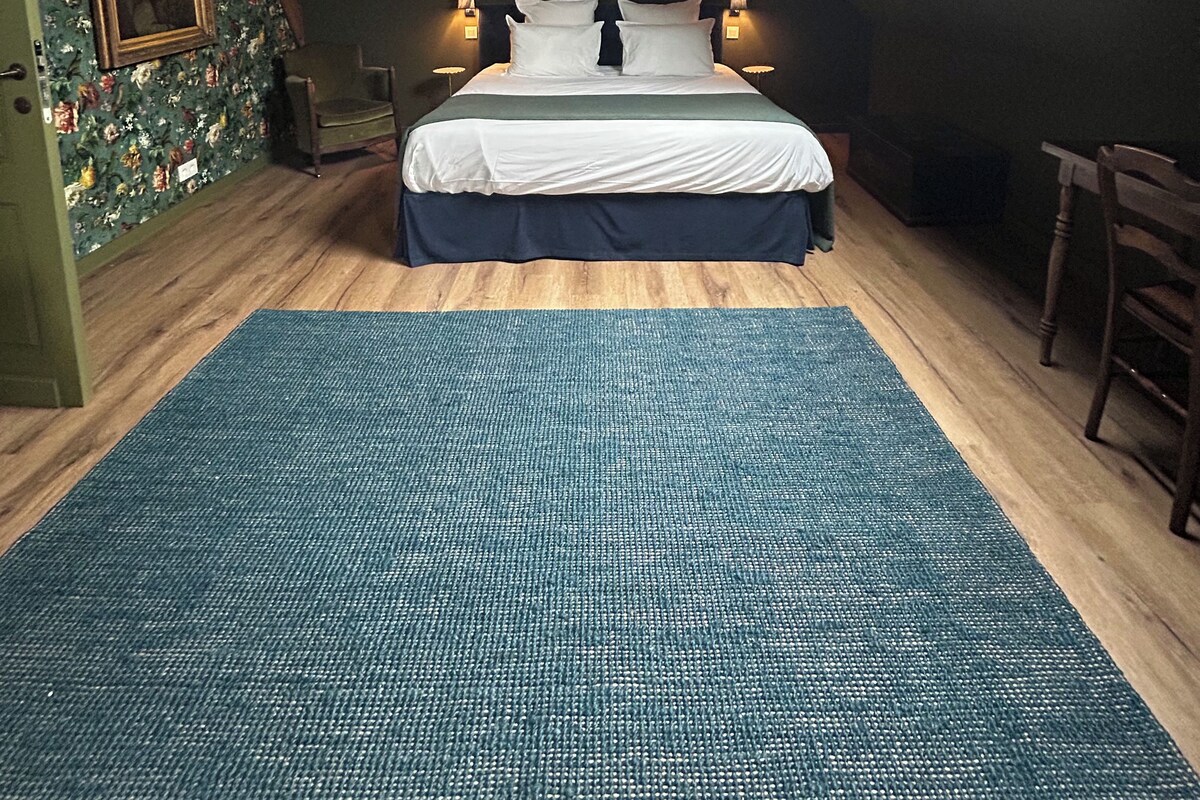 Quarto com teto inclinado, claraboia, cama com roupa de cama branca, duas luminárias fixadas na parede e piso de madeira.