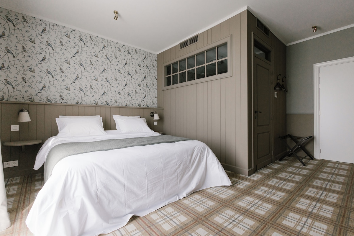 Quarto com cama, mesa de cabeceira, janela e porta.