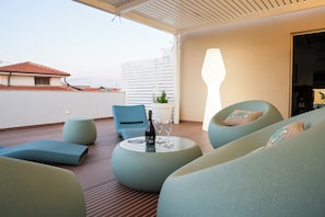 Uma área externa moderna com assento, uma mesa, cadeiras e uma garrafa de vinho.
