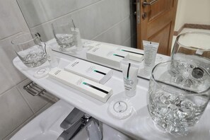 Uma bancada de banheiro com artigos de higiene pessoal, um copo de água e um copo de bebida alcoólica.