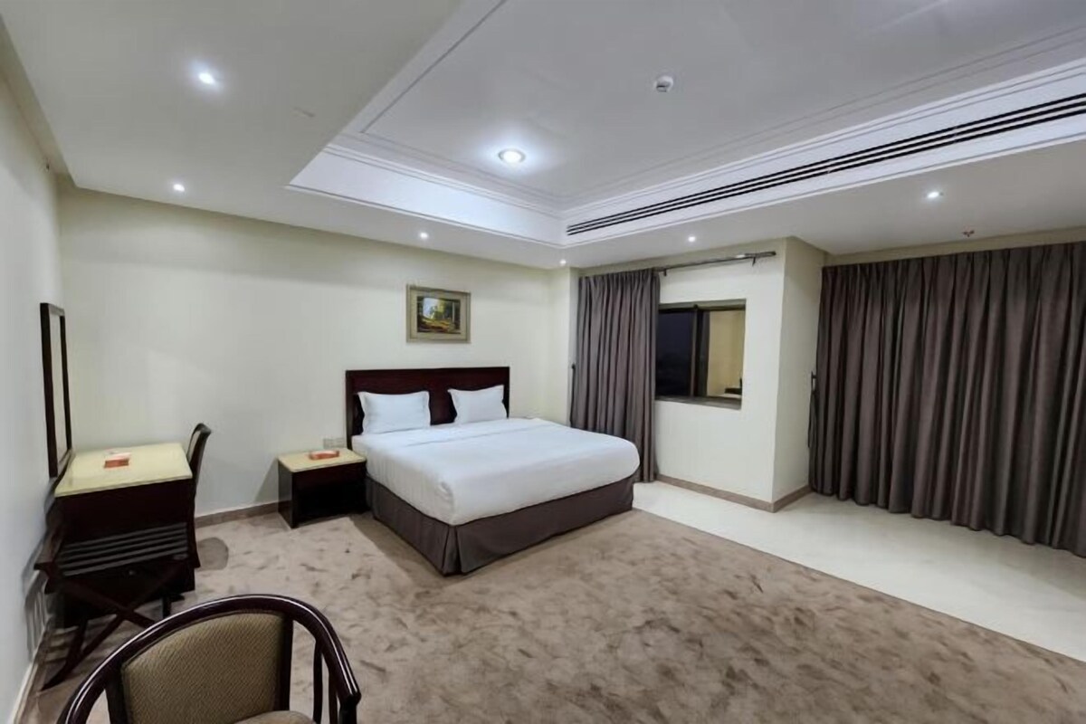 Quarto de hotel com uma cama grande, uma escrivaninha, uma cadeira e uma janela com cortinas.