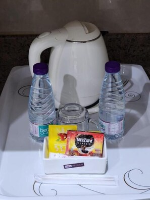 Uma chaleira branca, duas garrafas de água, um copo e uma embalagem de café Nescafe Classic sobre um tabuleiro branco.
