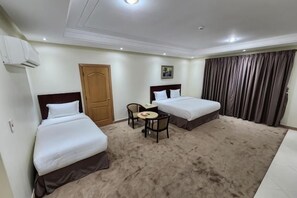 Quarto de hotel com duas camas, uma mesinha, uma cadeira e uma porta.