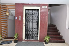 Entrada de um edifício com um portão de metal, escadas e duas plantas em vasos.