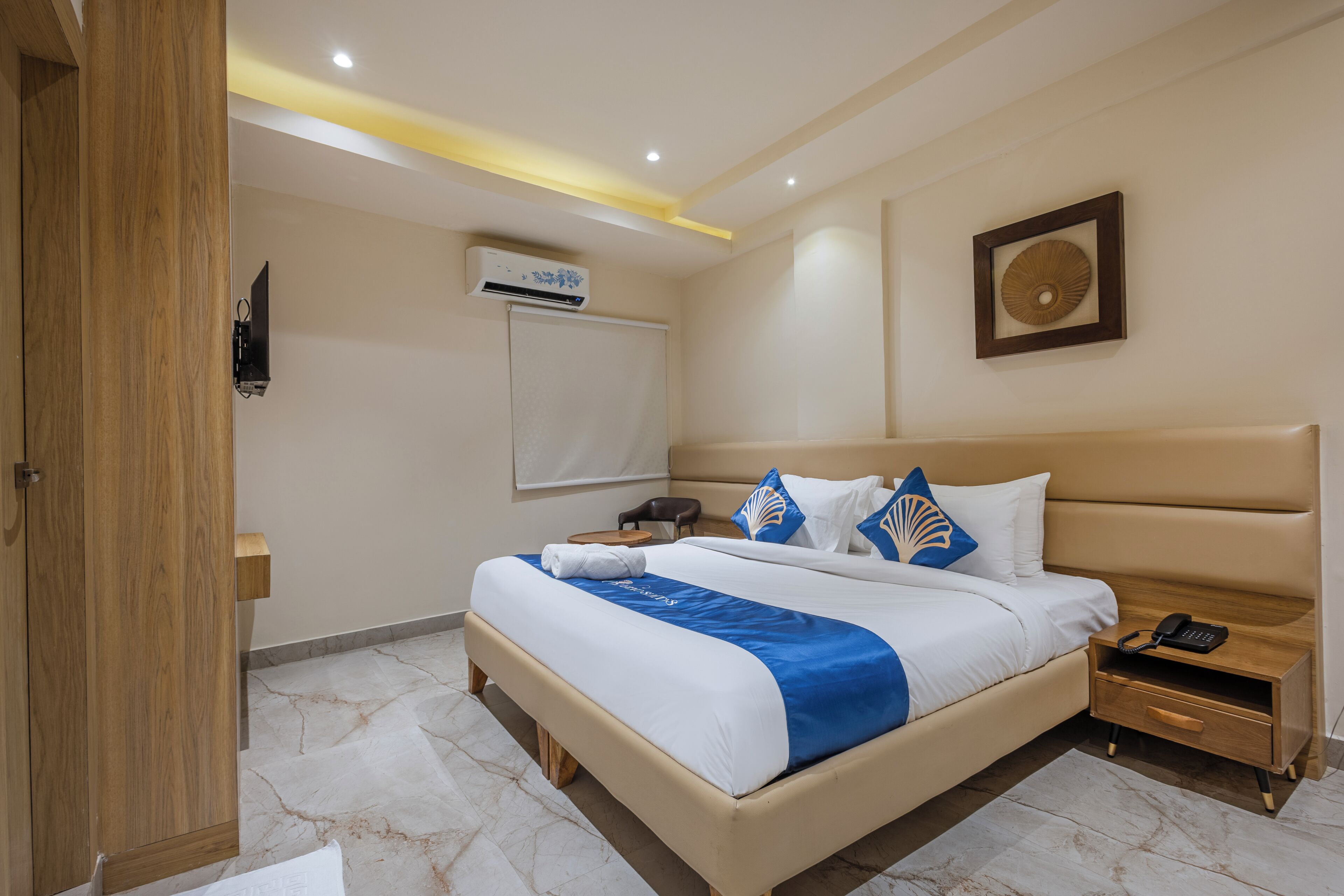 Quarto de hotel com uma cama grande, mesas de cabeceira, uma escrivaninha, um ar condicionado e uma obra de arte na parede.