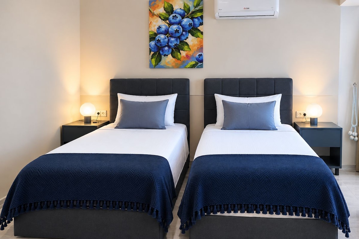 Quarto de hotel com duas camas, um quadro de mirtilos, ar-condicionado fixado na parede e abajures.