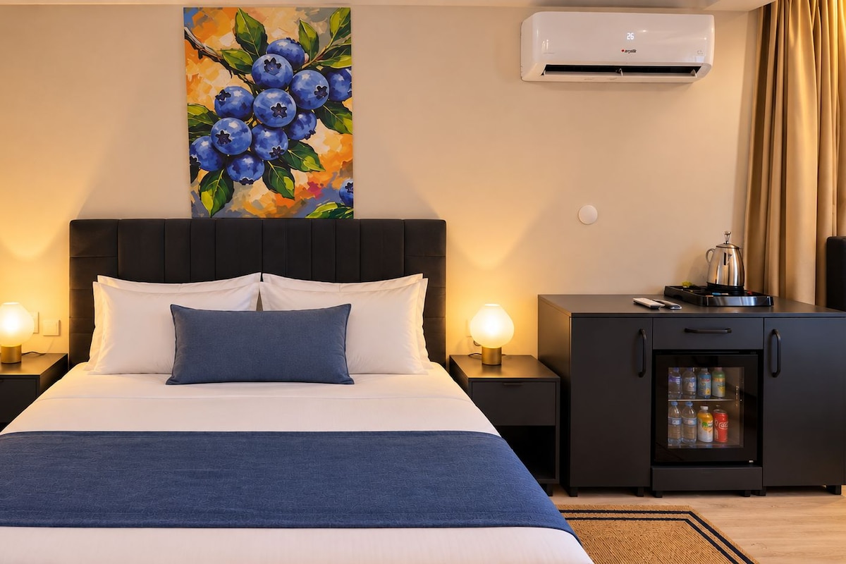Quarto de hotel com cama, luminárias laterais, minibar e aparelho de ar condicionado.