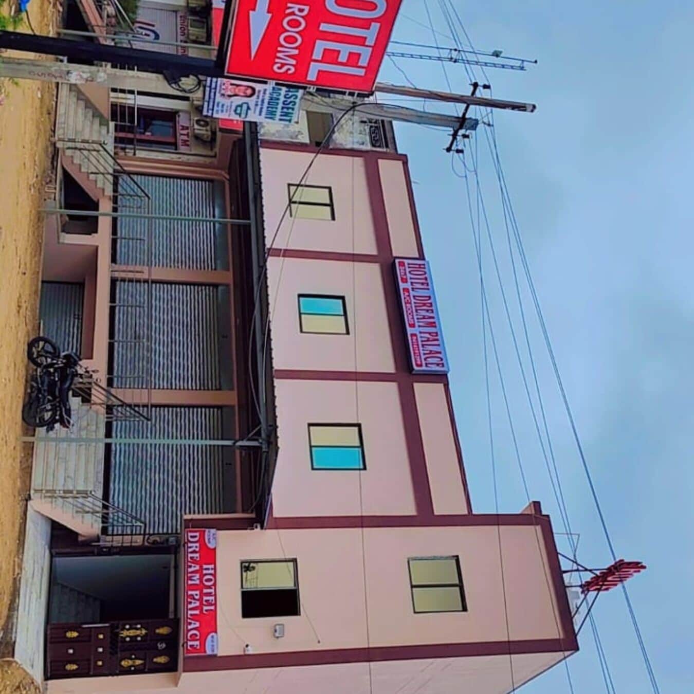 Um edifício de vários andares com uma placa indicando 'HOTEL DREAM PALACE' e outra placa para 'ROOMS', sinalizando acomodações disponíveis.