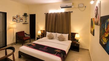 Quarto de hotel com uma cama, duas mesas de cabeceira, uma cadeira, ar condicionado e obras de arte nas paredes.