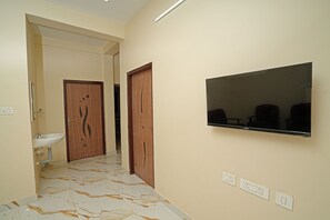 Corredor com pia, duas portas, TV fixada na parede e piso de mármore.