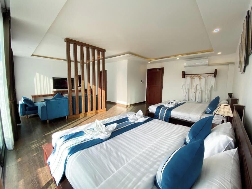 Quarto de hotel com duas camas, um espaço de estar e uma televisão.