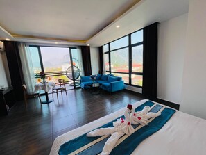 Quarto de hotel com uma cama grande, um sofá azul, uma mesa pequena com um vaso e uma varanda com vista.