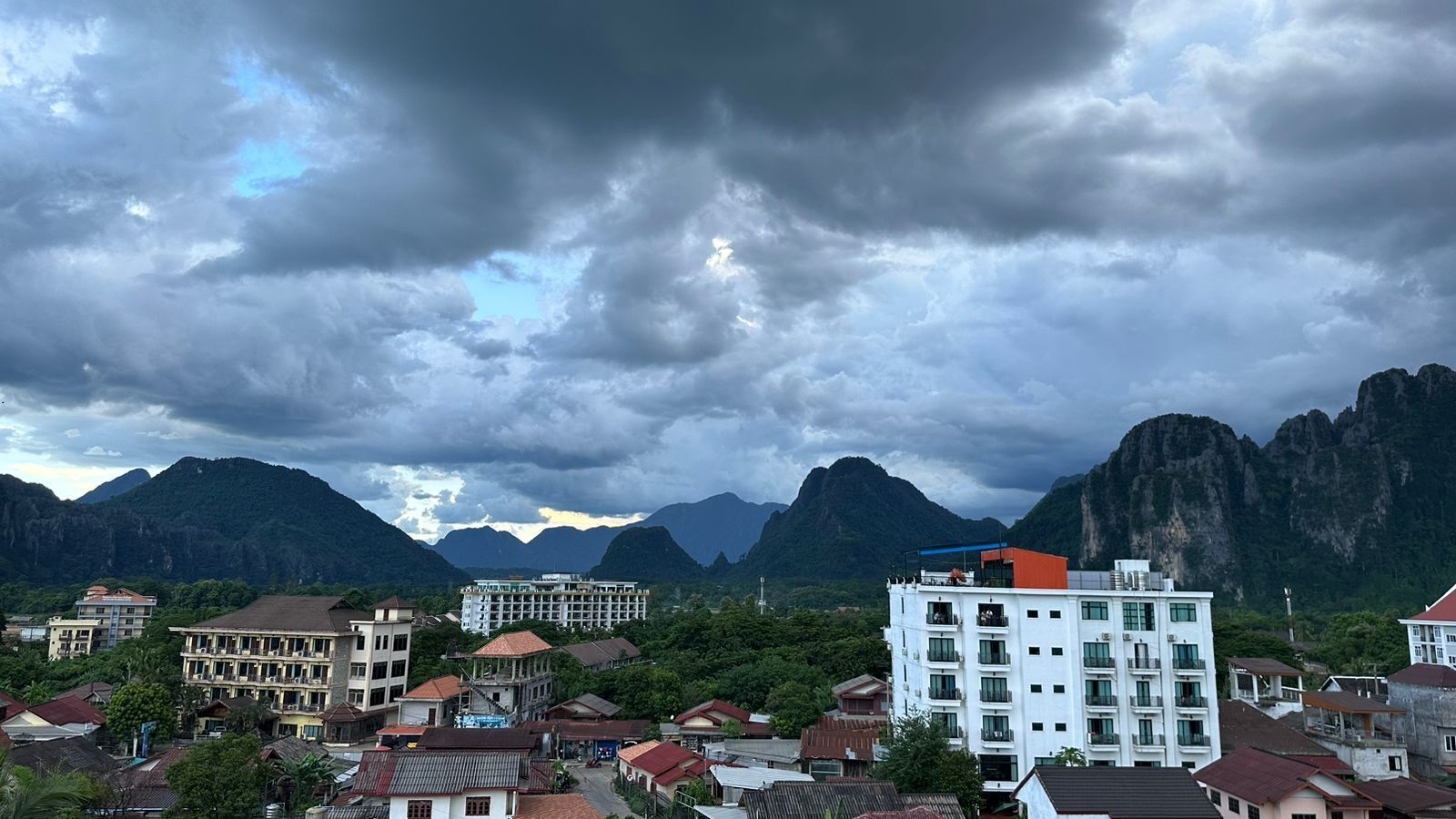 Zona residencial com edifícios altos, rodeada por montanhas e sob um céu nublado.