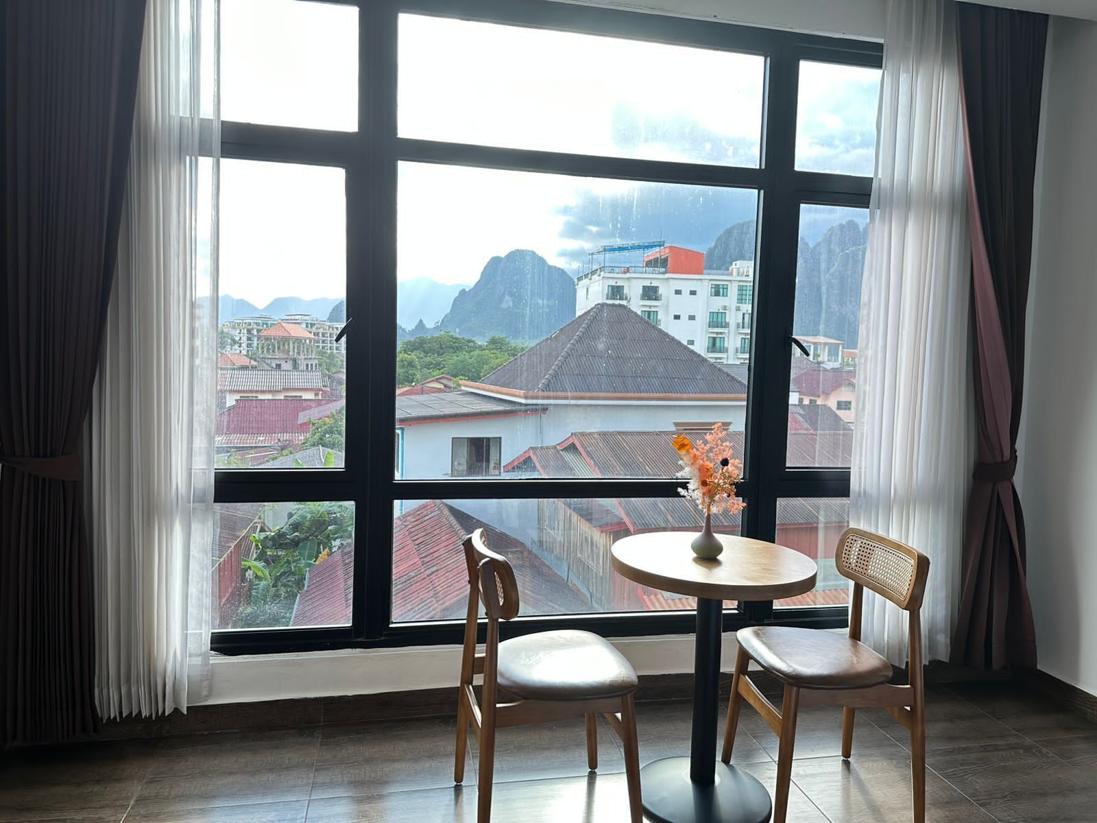 Quarto com uma janela grande, duas cadeiras e uma pequena mesa com um vaso.
