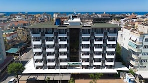 Um hotel com vários andares e um pátio central, rodeado por outros edifícios, com vista para o mar.
