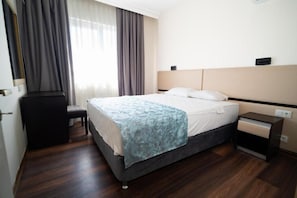 Quarto de hotel com cama, mesa de cabeceira, cadeira e escrivaninha.