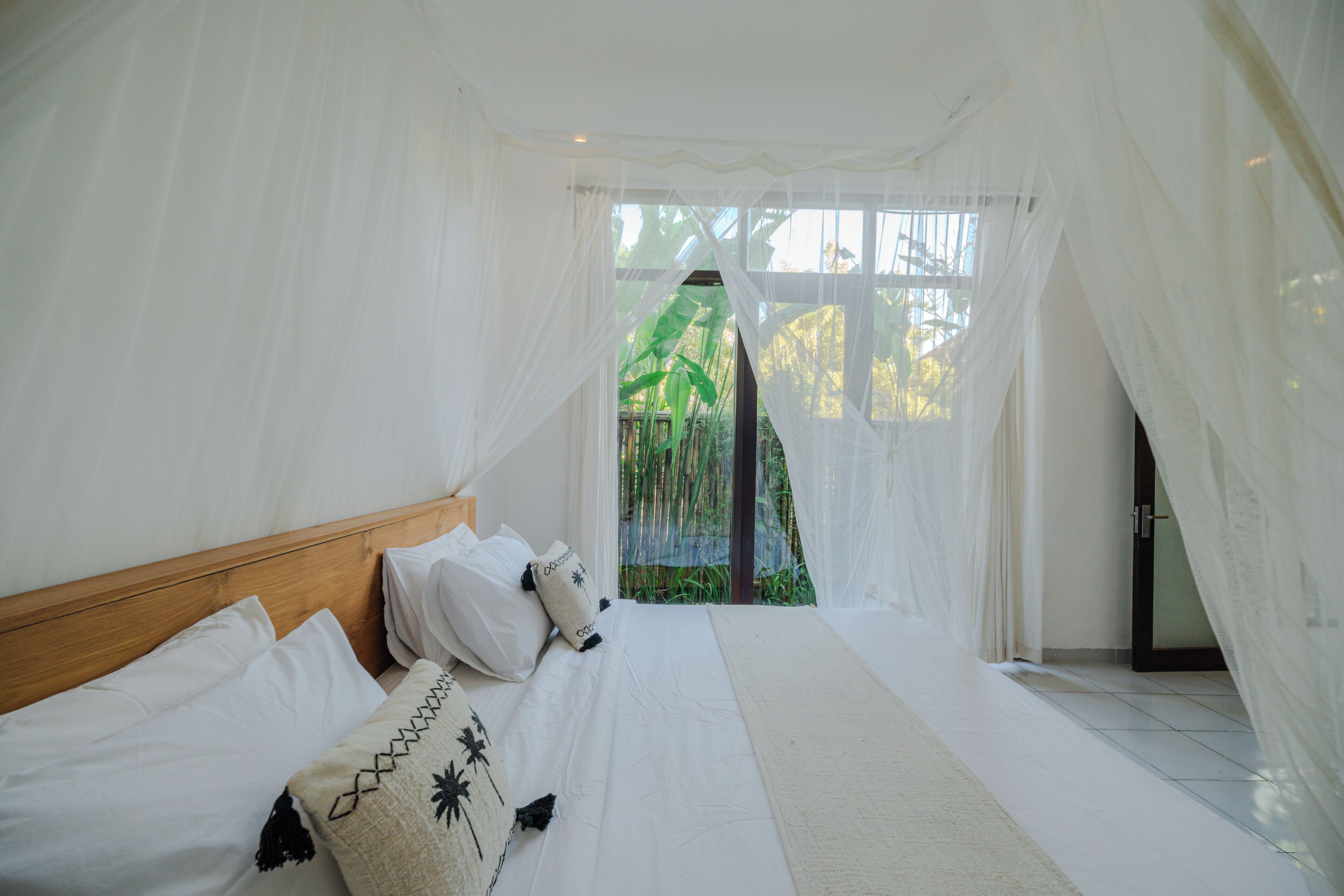 Quarto com uma cama grande, cortinas leves e vista para o verde lá fora.