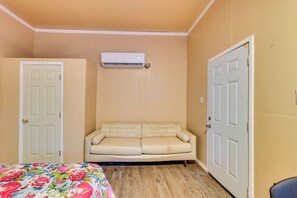 Quarto com sofá bege, colcha estampada e unidade de ar condicionado na parede.