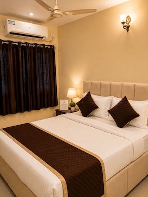 Quarto de hotel com cama, mesa de cabeceira, luminária, iluminação embutida na parede, ar condicionado e ventilador de teto.