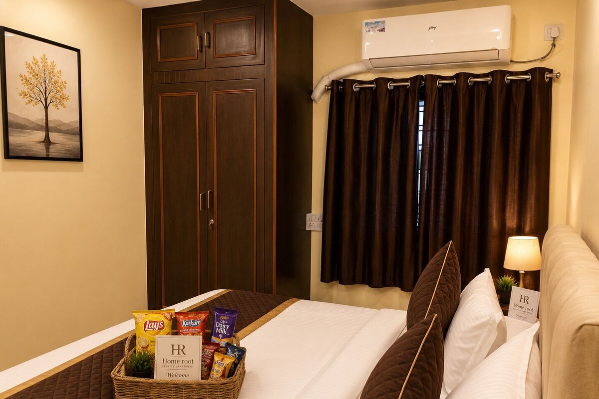 Quarto de hotel com uma cama, mesa de cabeceira com abajur, guarda-roupa de madeira escura, quadro na parede e janela com cortinas.