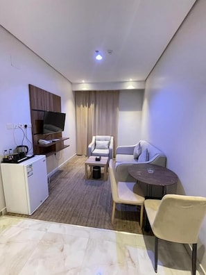 Quarto de hotel pequeno, com televisão de tela plana, sofá, mesa de jantar compacta e cozinha americana.