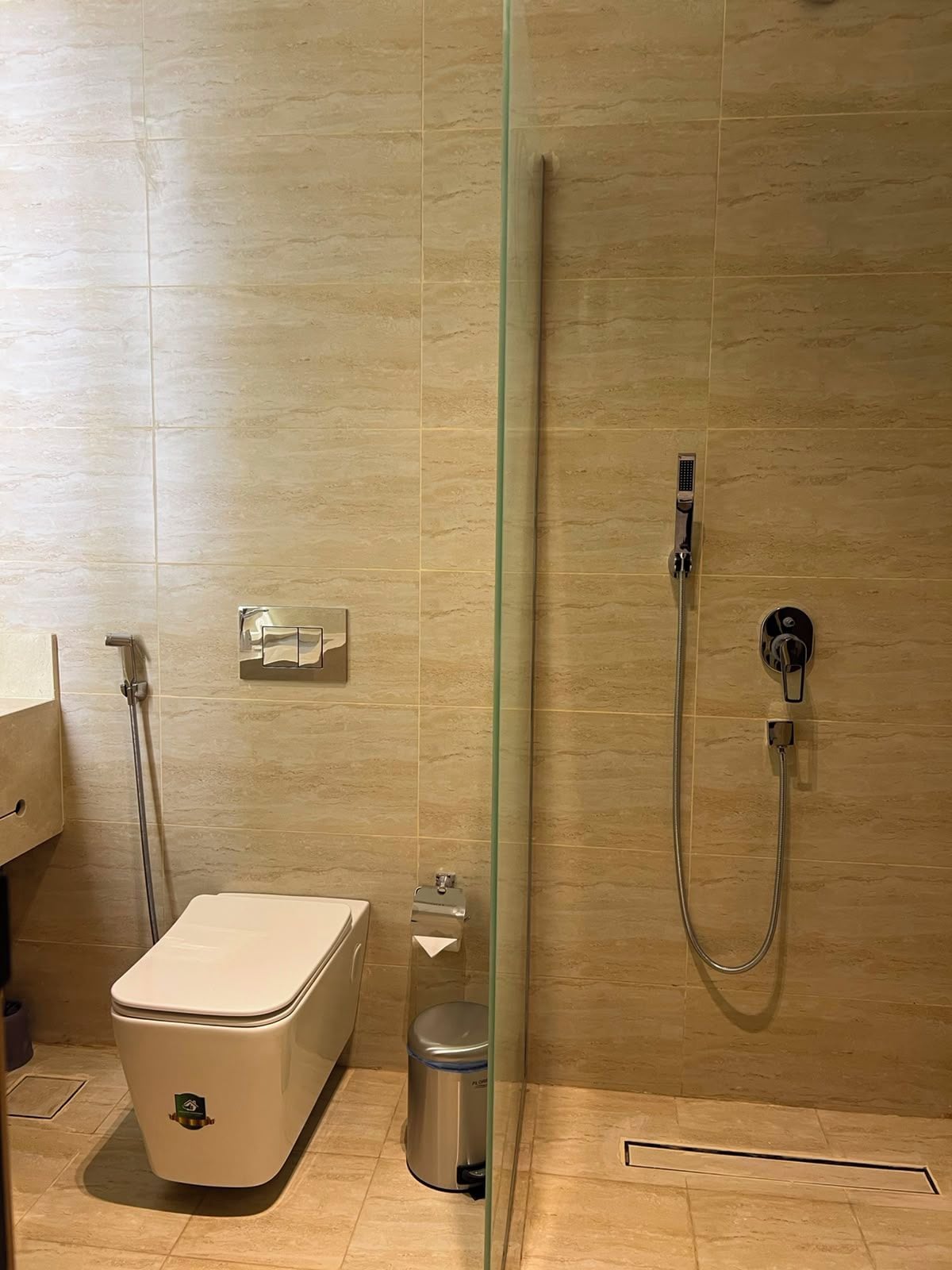 Casa de banho com sanita, um cesto de lixo, chuveiro com divisória de vidro e um porta-toalhas.