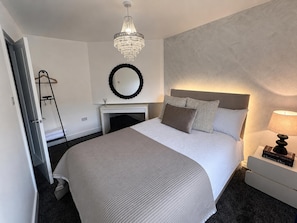 Quarto de hotel com uma cama grande, abajur, espelho, lareira e um candelabro.