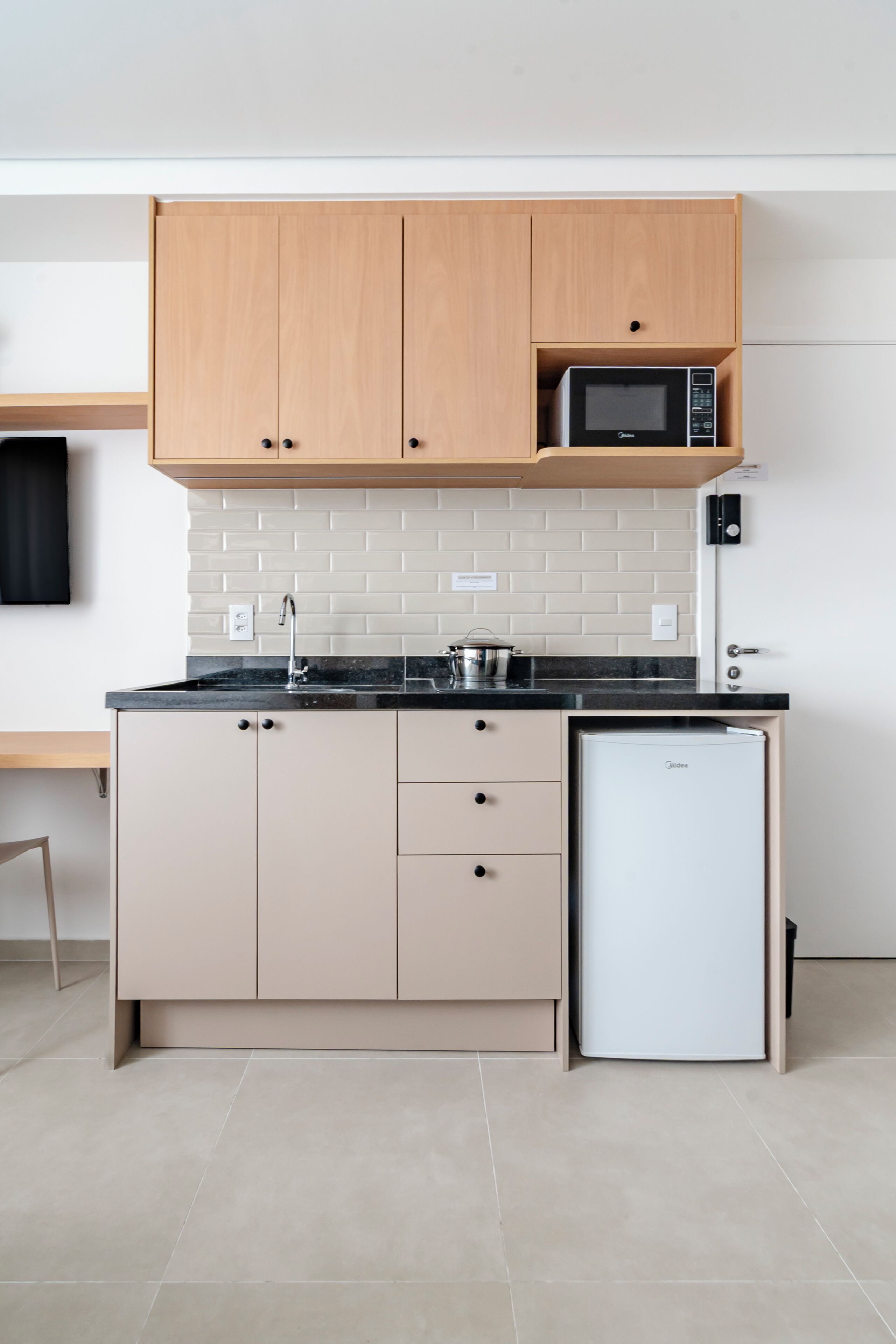 Cozinha compacta com armários de madeira, micro-ondas embutido, pia e um refrigerador pequeno.