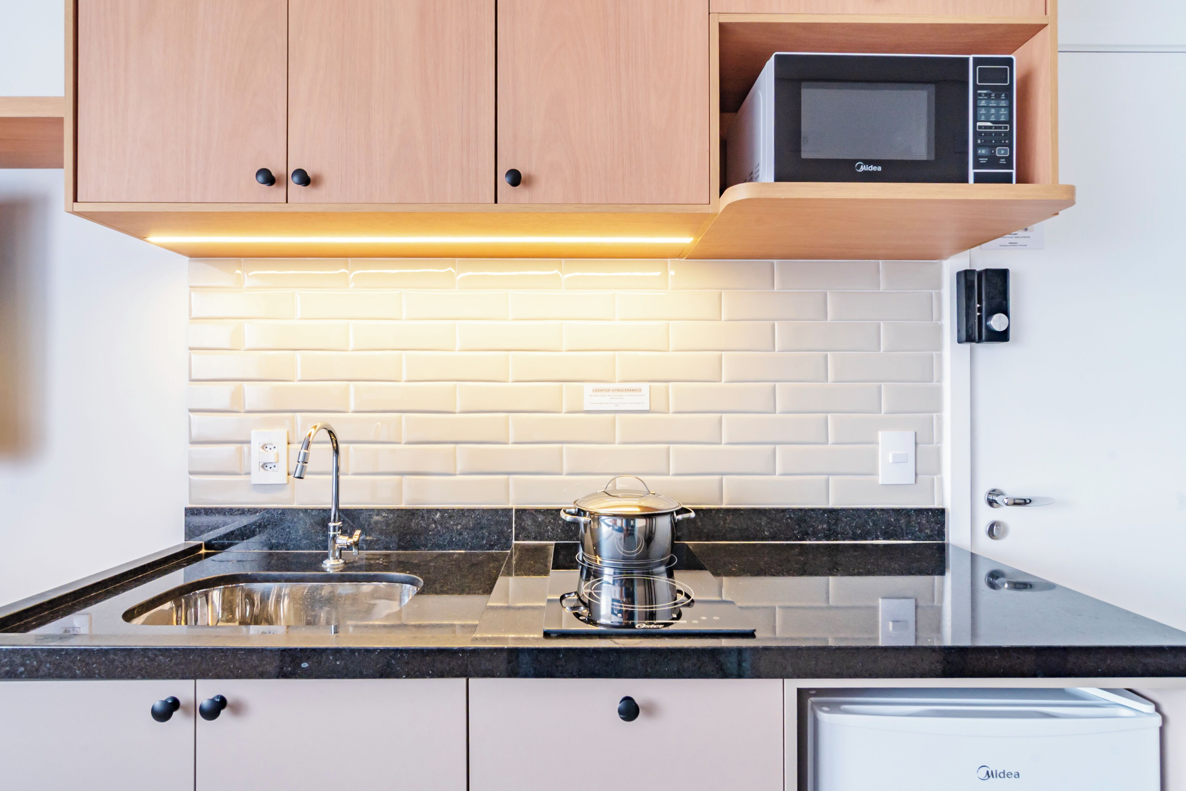 Cozinha moderna com micro-ondas embutido, pia de aço inoxidável e fogão.