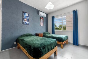 Quarto com duas camas de madeira, parede cinza com textura e janela com cortinas azuis.