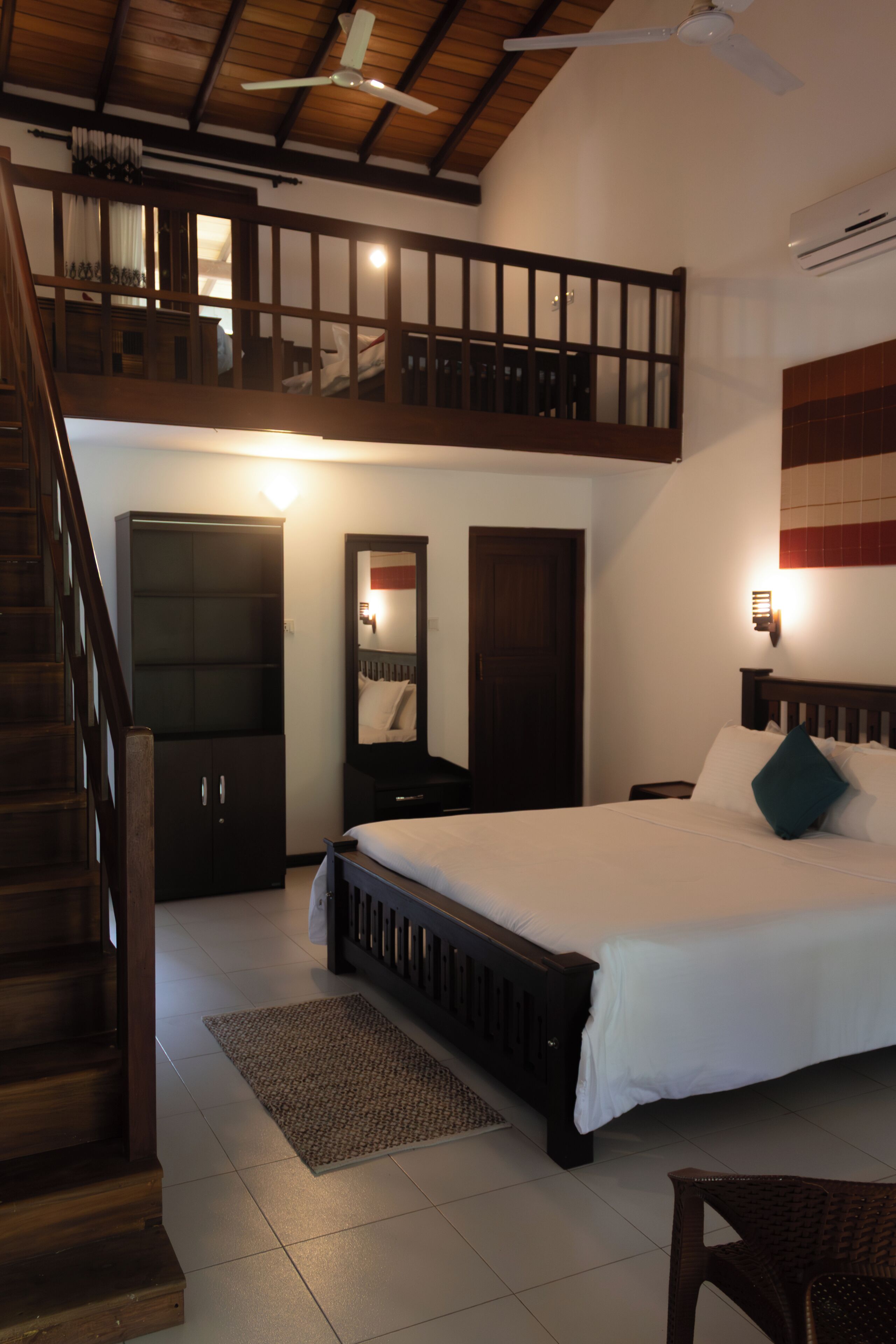Quarto com cama, escrivaninha, cadeira, guarda-roupa, espelho e escada que dá para um andar superior.