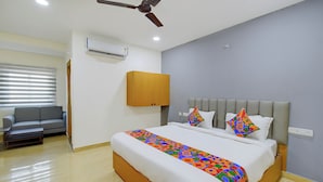 Quarto de hotel com cama, ventoinha no teto, aparelho de ar condicionado, sofá e janela com persianas.