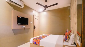Quarto de hotel com cama, televisão na parede, ventoinha no teto e espelho com cortinas.