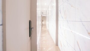 Corredor com uma porta à esquerda e paredes de mármore à direita.