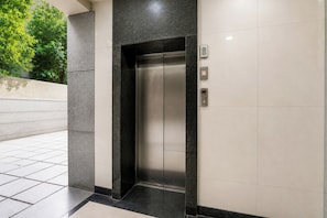 Um elevador com acabamento metálico, embutido em uma parede com azulejos estampados e uma base escura contrastante.