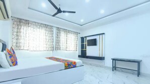 Quarto moderno com cama, ventilador de teto, TV e um banco.